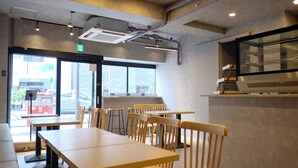 Interior de restaurante com mesas e cadeiras de madeira, janelas amplas e área externa visível.
