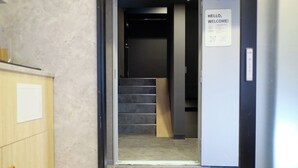 Entrada de hotel com um letreiro que diz 'HELLO, WELCOME!', escadaria que leva ao andar superior e um tapete com a inscrição 'LUMA URBAN HOTEL' na base.