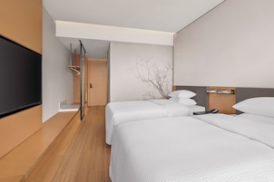 Quarto de hotel moderno com duas camas, televisão de tela plana, mesa de cabeceira com abajur e TV na parede.