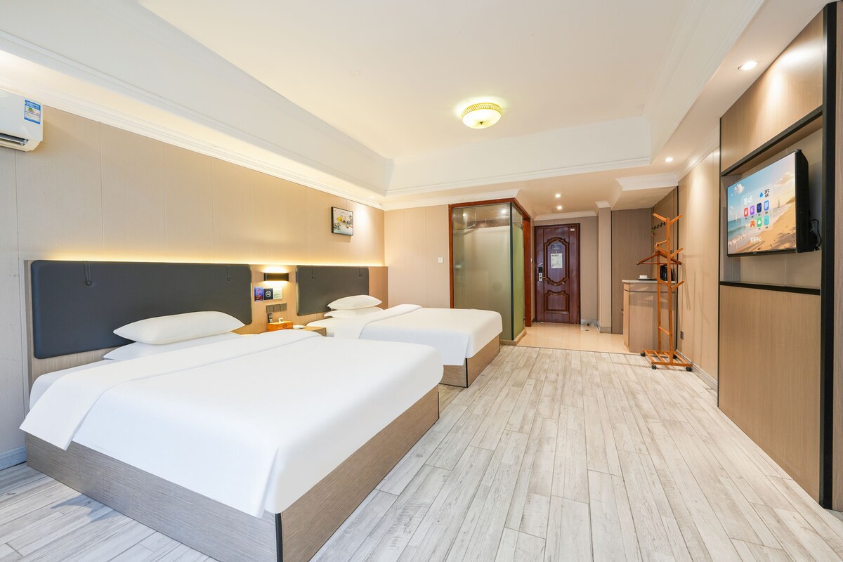 Quarto de hotel com três camas, uma televisão, um cabideiro e um espelho.