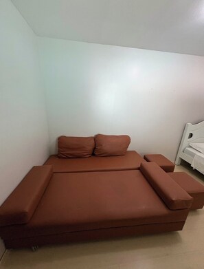 Quarto individual com uma cama de molas marrom, mesa de cabeceira e cabeceira branca.