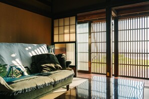 Um quarto japonês tradicional com tatames, uma mesa de madeira baixa, um sofá com almofadas e portas deslizantes shoji.