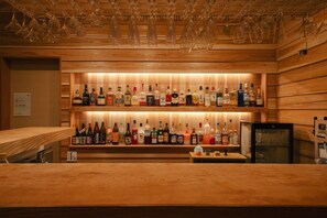 Uma área de bar com prateleiras de madeira exibindo diversas garrafas de bebidas e um suporte para vinhos suspenso.