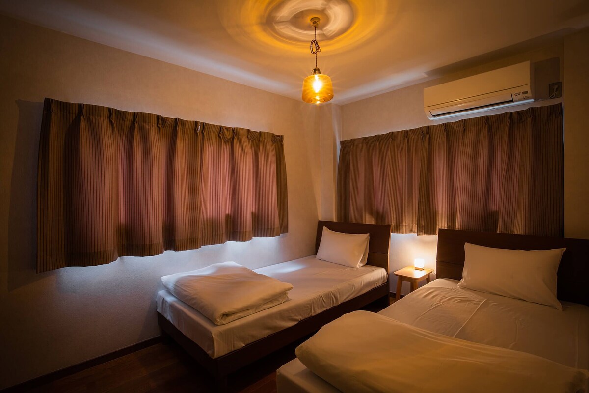 Quarto de hotel com duas camas, uma lâmpada no teto, ar condicionado e cortinas.