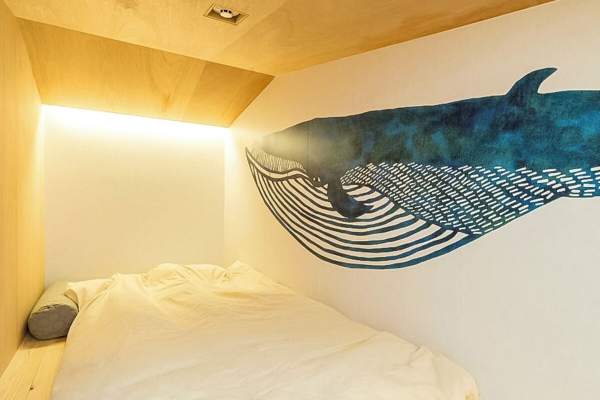 Quarto com cama, luminária fixada na parede e um grande mural de baleia.