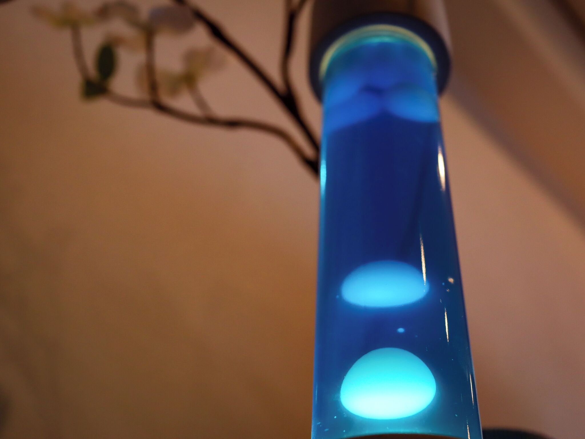 Recipiente de vidro vertical com líquido azul e esferas flutuantes.