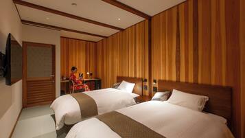 Quarto de hotel com duas camas, painéis de madeira, uma escrivaninha com cadeira e uma televisão fixada na parede.