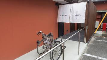 Uma cadeira de rodas estacionada ao lado de um corrimão, entrada de um edifício e um banner com texto.