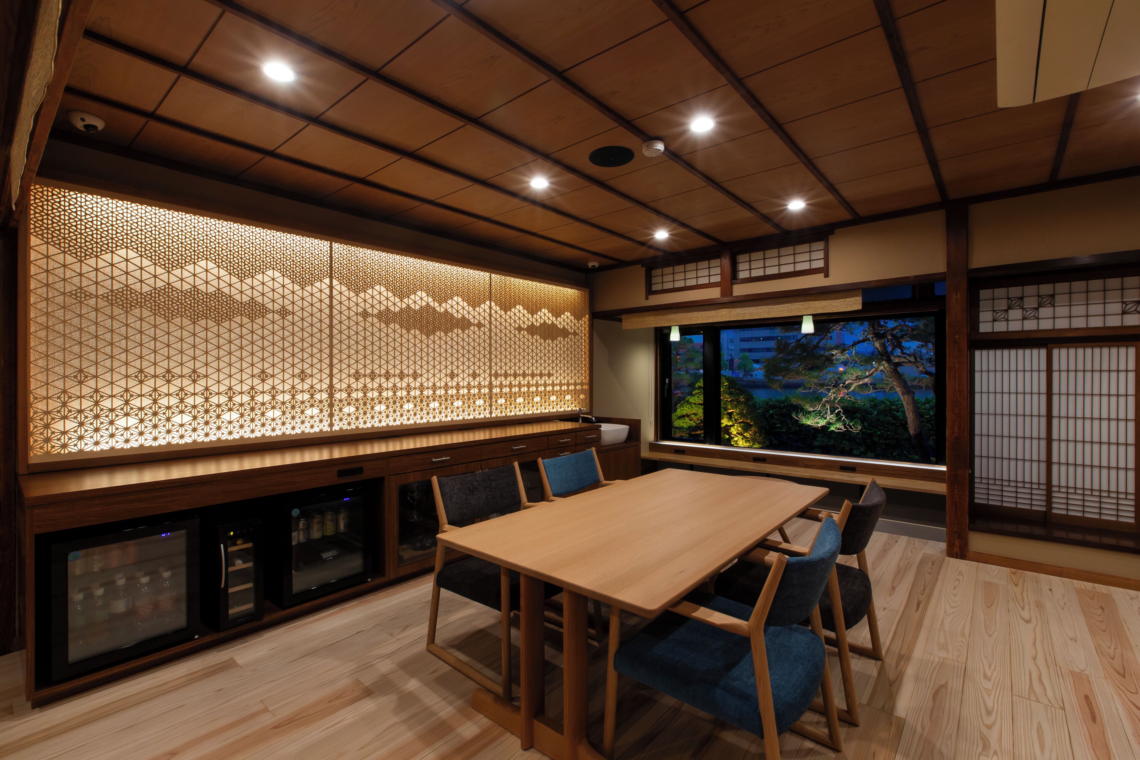 Um quarto japonês tradicional com tatames, uma mesa baixa e vista para a natureza através de uma janela.