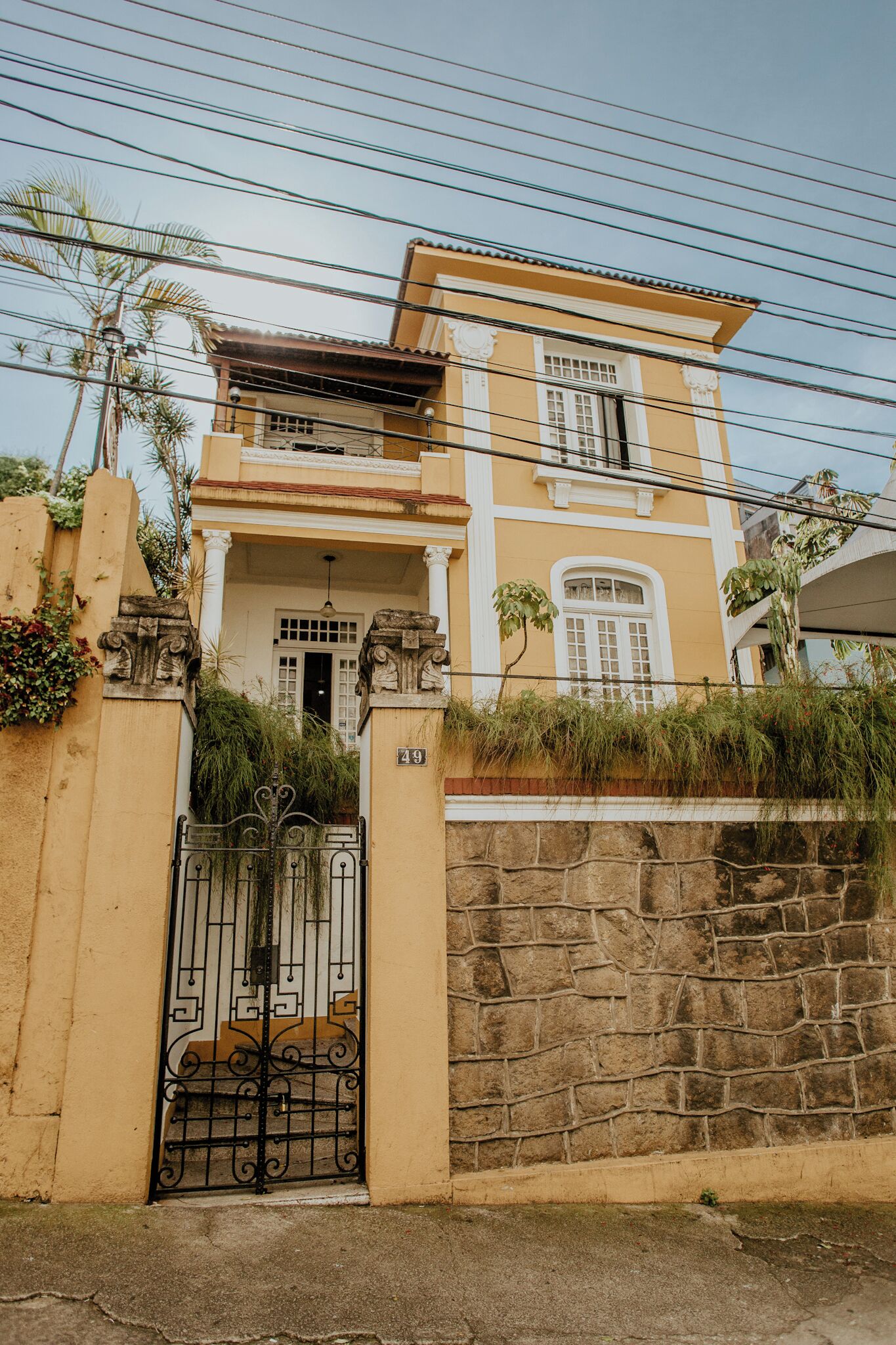 Um edifício de dois andares com parede de pedra, um portão de metal e o número 49 na parede.