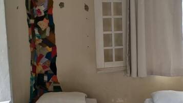 Um pequeno alojamento de um único quarto, com cama, janela com cortinas e um mural na parede.