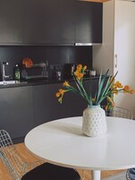 Uma cozinha moderna com armários escuros, uma mesa de jantar branca e um vaso com flores.
