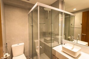 Uma casa de banho moderna com chuveiro em cabine de vidro, lavatório branco e sanita.