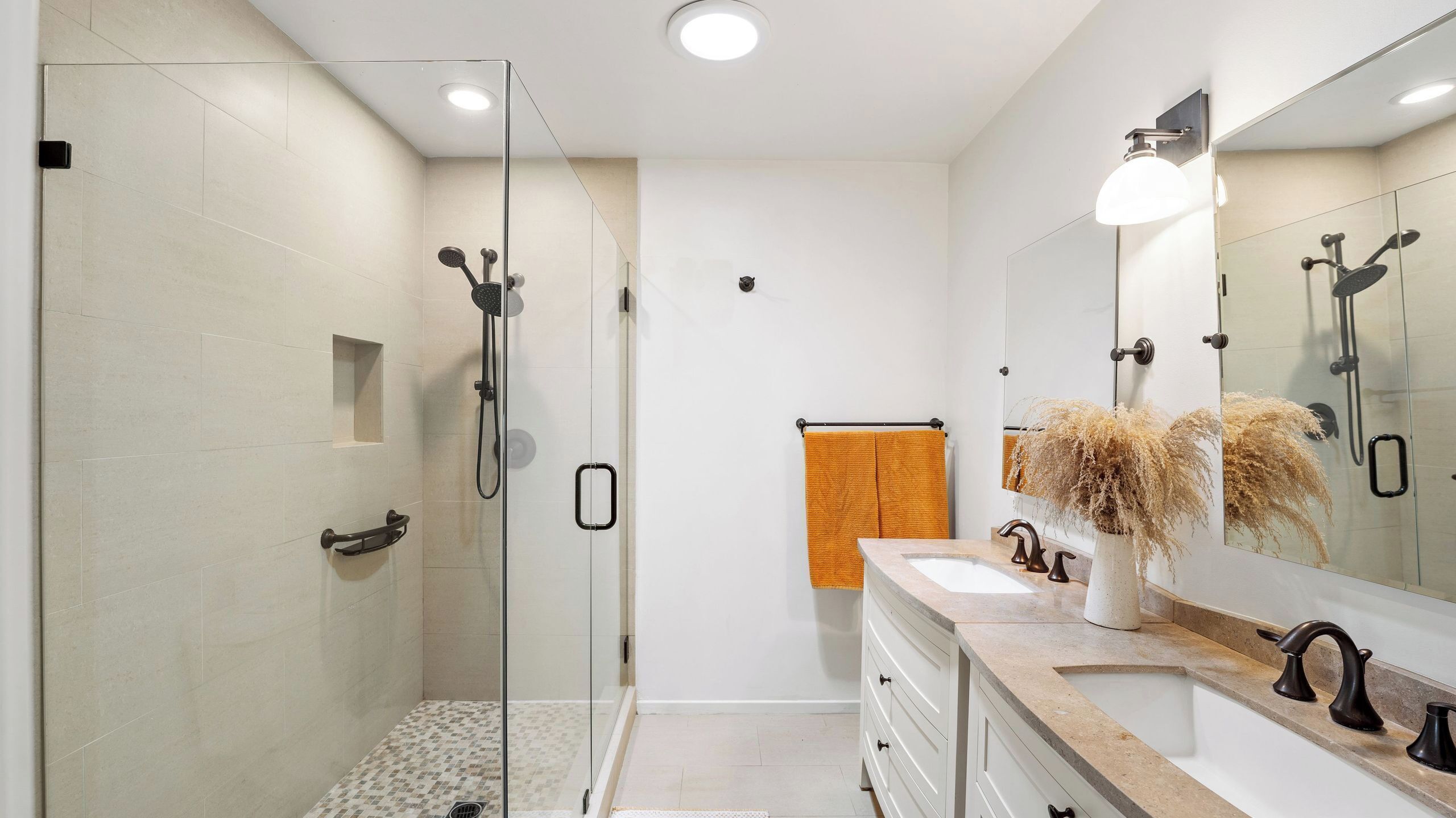 Uma casa de banho moderna com cabine de duche em vidro, toucador branco com espelho e um porta-toalhas com toalha amarela.