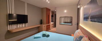 Quarto de hotel com uma cama, televisão presa na parede, um espelho e um quadro de um penhasco.
