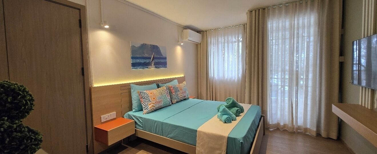 Quarto de hotel com cama, mesa de cabeceira, televisão e janela com cortinas.