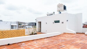 Um terraço no telhado com uma parede branca, um reservatório de água e um corrimão de metal.