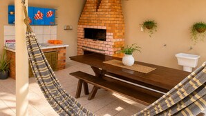 Uma cozinha ao ar livre rústica, com forno de tijolos, mesa de madeira e rede.