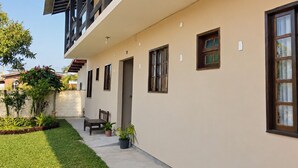 Um edifício de dois andares com um alpendre coberto, um pequeno jardim e um banco.