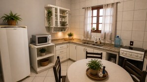 Cozinha compacta com geladeira, micro-ondas, pia e fogão. Há uma mesa de jantar com cadeiras e um vaso de planta sobre ela.