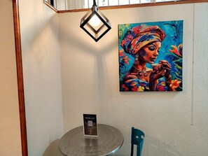 Quarto com mesa redonda, cadeira azul, luminária pendente e quadro na parede.
