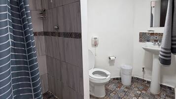 Casa de banho com chuveiro, sanita e lavatório, e chão estampado.