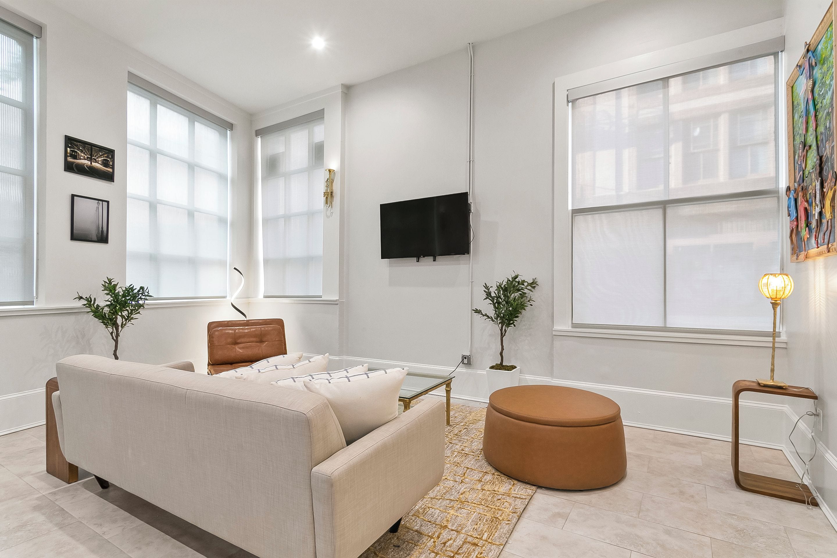 Quarto moderno com cama, mesa de cabeceira, televisão e duas janelas.
