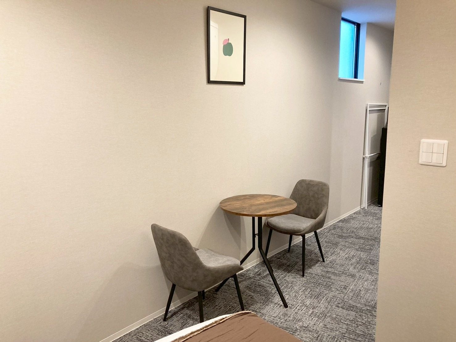 Um quarto pequeno com uma mesa redonda e duas cadeiras, um quadro na parede e uma janela com vista.