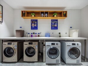 Uma lavanderia com quatro máquinas de lavar, uma prateleira com objetos decorativos e cartazes informativos.