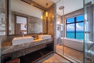 Uma casa de banho moderna com duas pias, um espelho grande e um chuveiro com divisória de vidro e vista para o oceano.