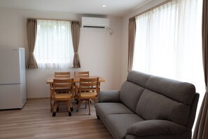 Uma sala de estar com sofá, mesa de jantar com cadeiras, ar-condicionado e geladeira.