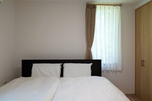 Um quarto com uma cama, uma janela com cortinas e um guarda-roupa.