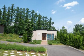 Um edifício moderno com porta de madeira, cercado por uma área arborizada.
