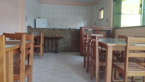 Uma área de refeições com mesas e cadeiras de madeira, painel de azulejos e uma geladeira.