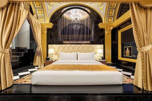 Um quarto de hotel luxuoso com uma cama grande, detalhes dourados elaborados e um candelabro.