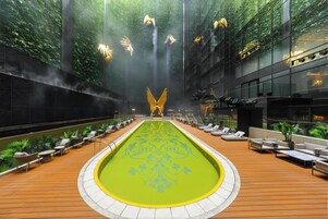 Uma área de piscina com design central, rodeada por assentos e vegetação.