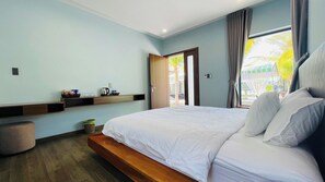 Quarto de hotel com cama, uma mesinha com objetos, um cesto de lixo e uma janela com cortinas.