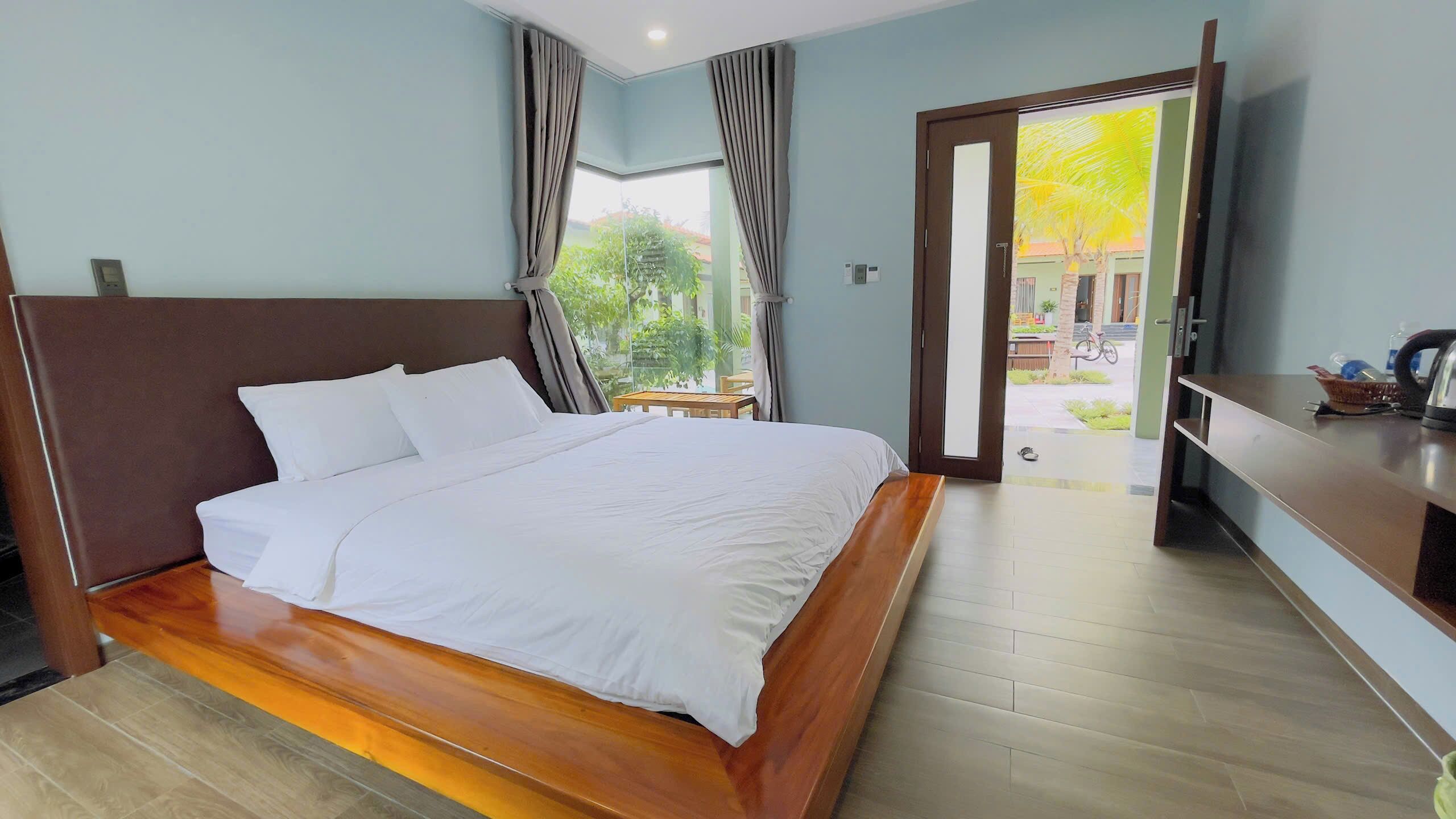 Quarto com cama de madeira, uma mesinha e vista para o exterior.