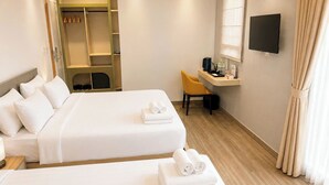 Quarto de hotel com duas camas, uma escrivaninha, uma cadeira, uma televisão e um guarda-roupa.
