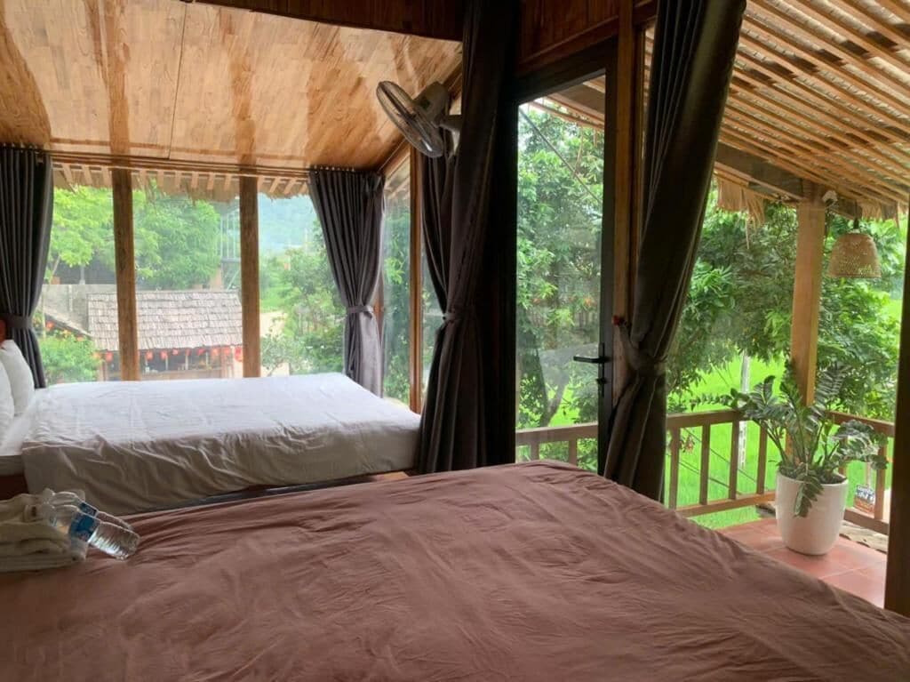 Quarto com cama, ventilador e vista para o verde lá fora.