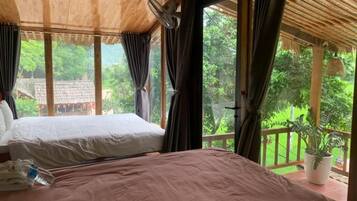 Quarto com cama, ventilador e vista para o verde lá fora.