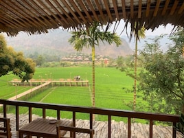 Uma construção com telhado de palha, com vista para um campo verde e edifícios ao longe.