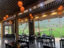 Um restaurante com mesas ao ar livre, vigas de madeira e lanternas penduradas.