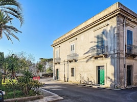Um edifício de dois andares com uma varanda, uma porta verde e céu claro.