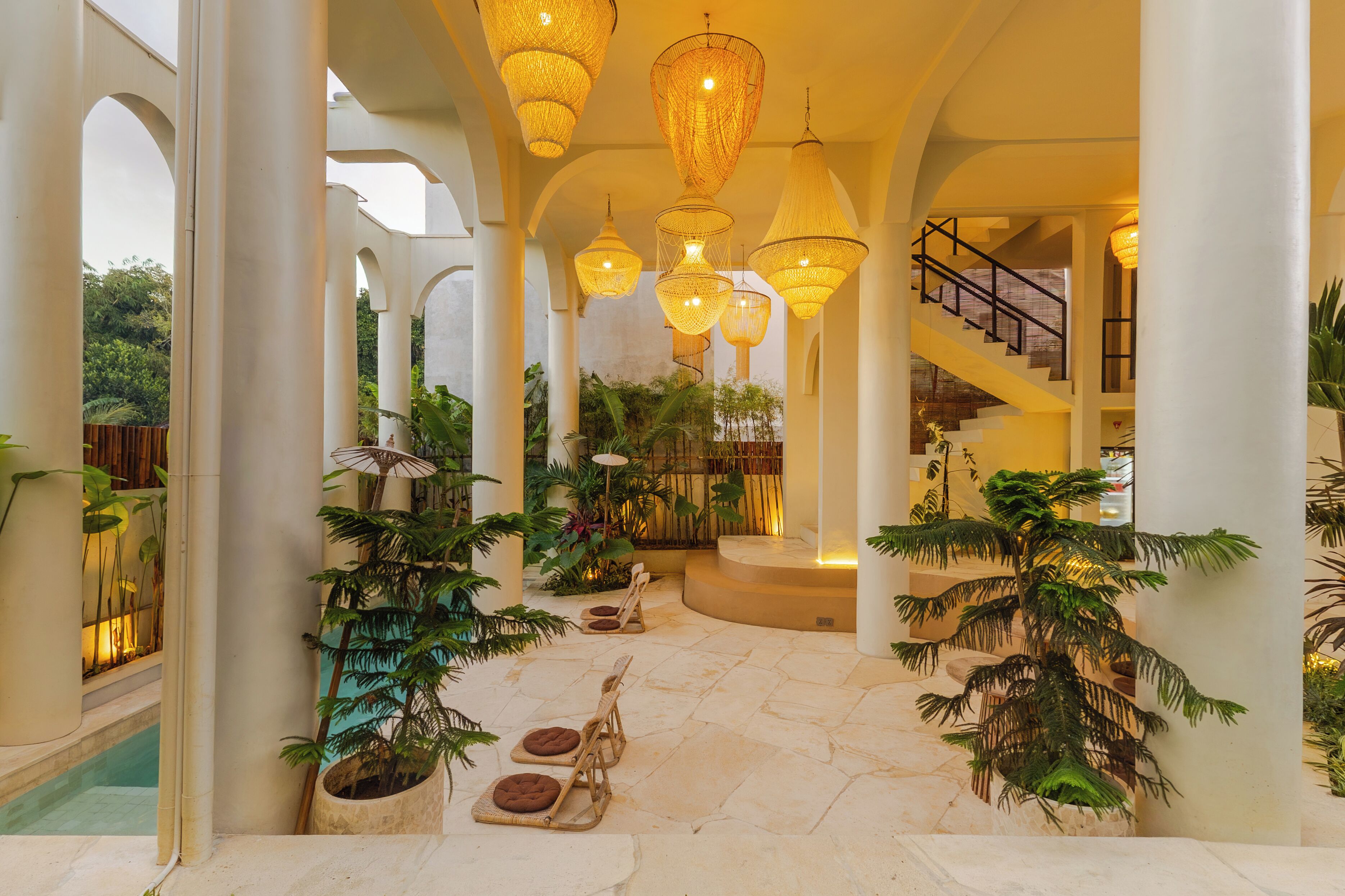 Um espaço amplo e coberto, com piscina, colunas e lustre de vime pendente.