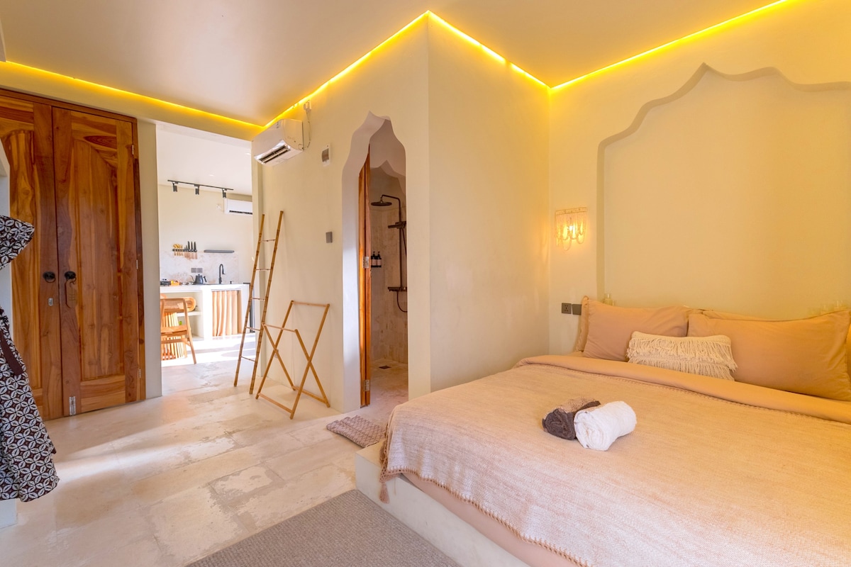 Quarto com cama, porta de madeira, banheiro e cozinha.