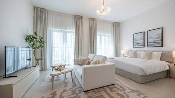 Quarto moderno com cama, sofá, televisão e planta.