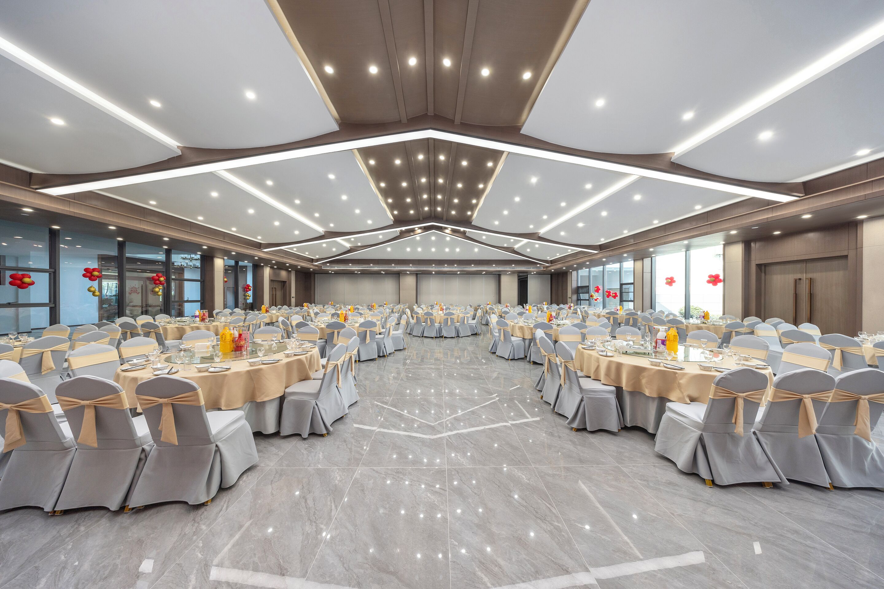 Um amplo salão de banquetes com mesas redondas, cadeiras cinzas e um design moderno no teto.
