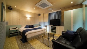 Quarto de hotel com cama, televisão, sofá e secretária com computador.
