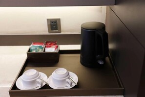 Uma bandeja com duas xícaras e pires brancos, uma cafeteira preta e uma caixa de saquinhos de chá.